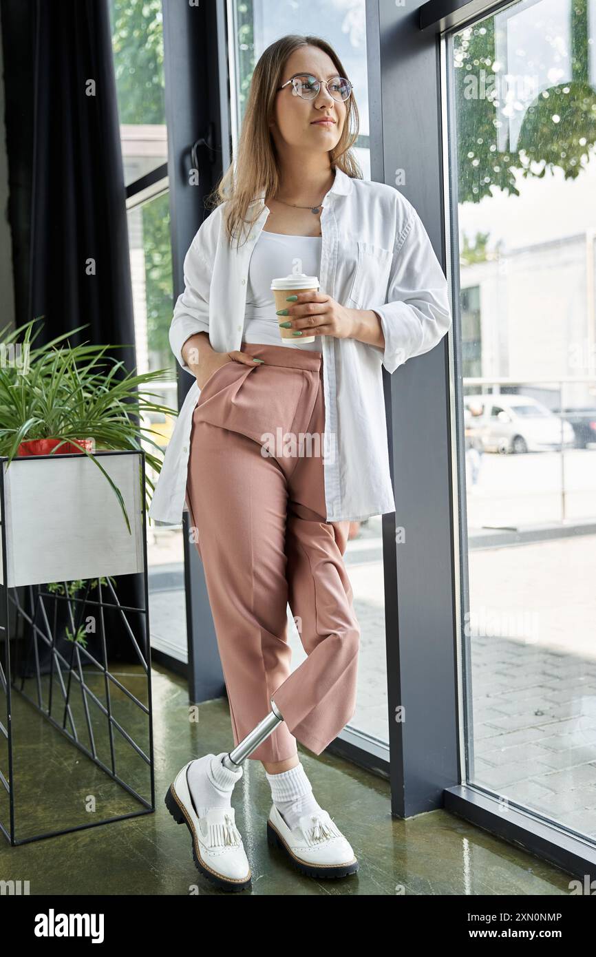 A woman with a prosthetic leg stands by a window, holding a cup of ...