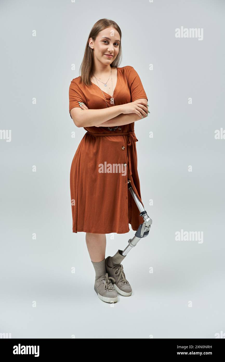 A woman with a prosthetic leg stands confidently in a brown dress, arms ...