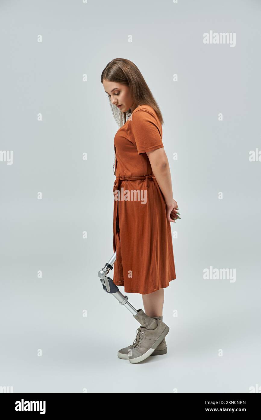 A woman wearing a brown dress stands with a prosthetic leg, her gaze ...