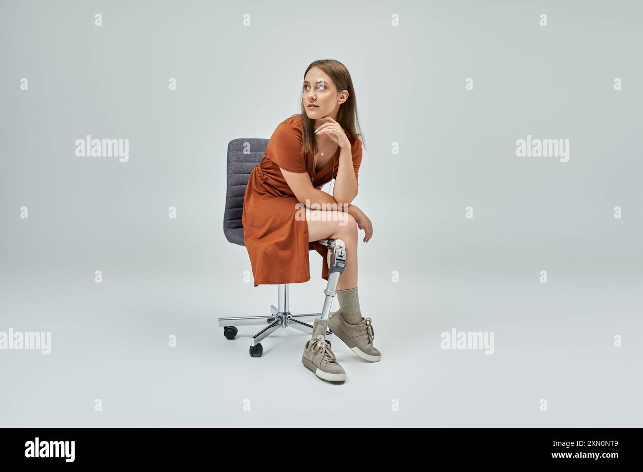 A woman with a prosthetic leg sits on a chair in a studio setting Stock ...