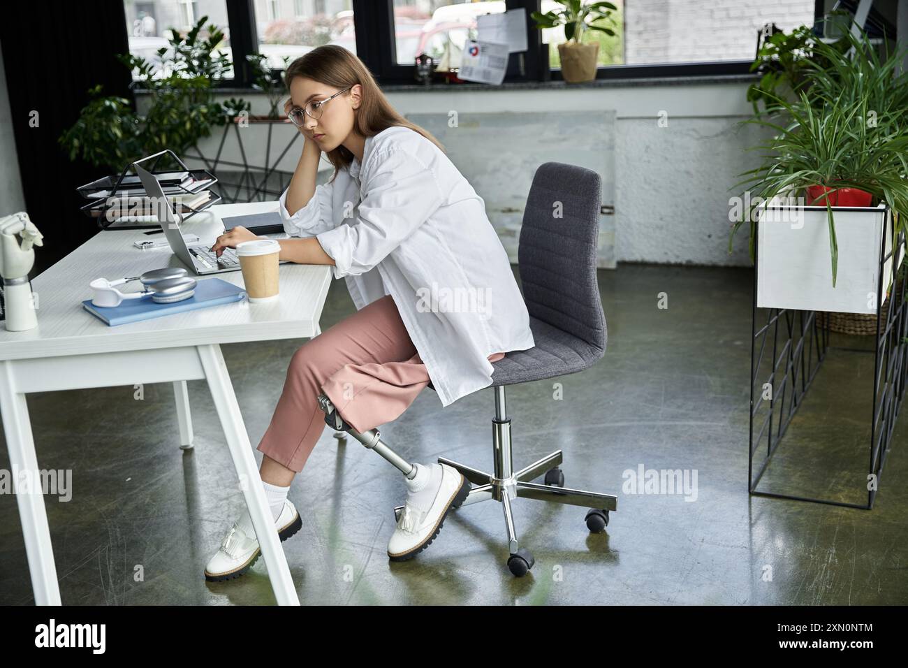 A woman with a prosthetic leg sits at a desk, working on a laptop Stock ...