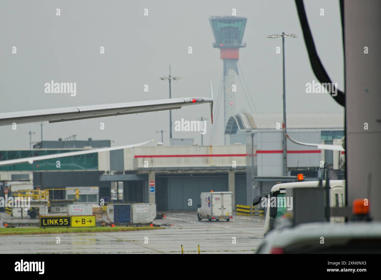 Heathrow airport on a misty day in May. Plane wing and support vehicles ...