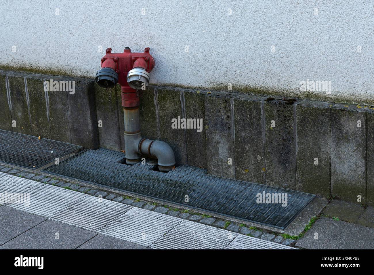 A red fire hydrant is secured to a concrete wall, with a metal pipe ...