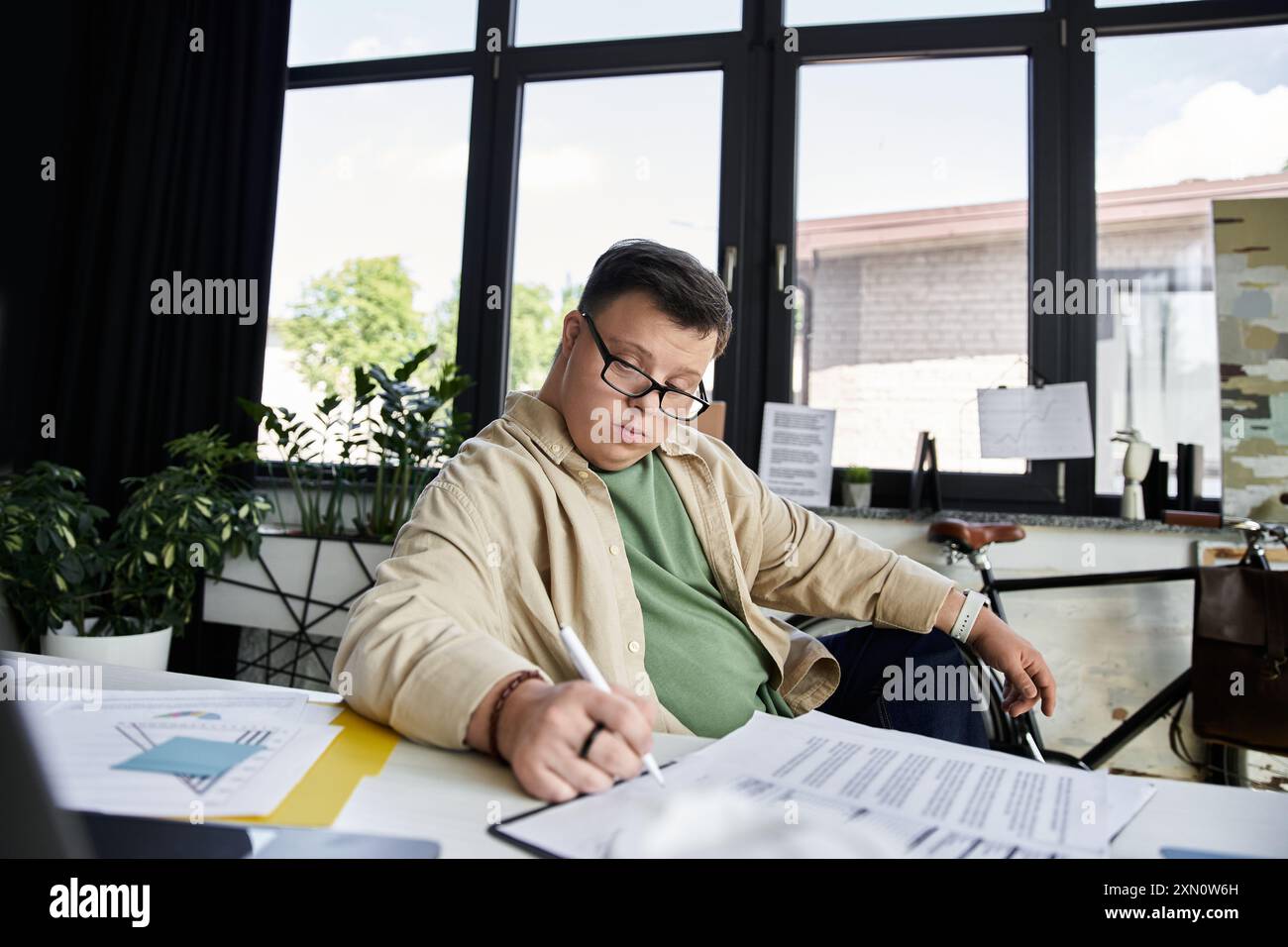 A young man with Down syndrome sits at a desk, focused on filling out ...