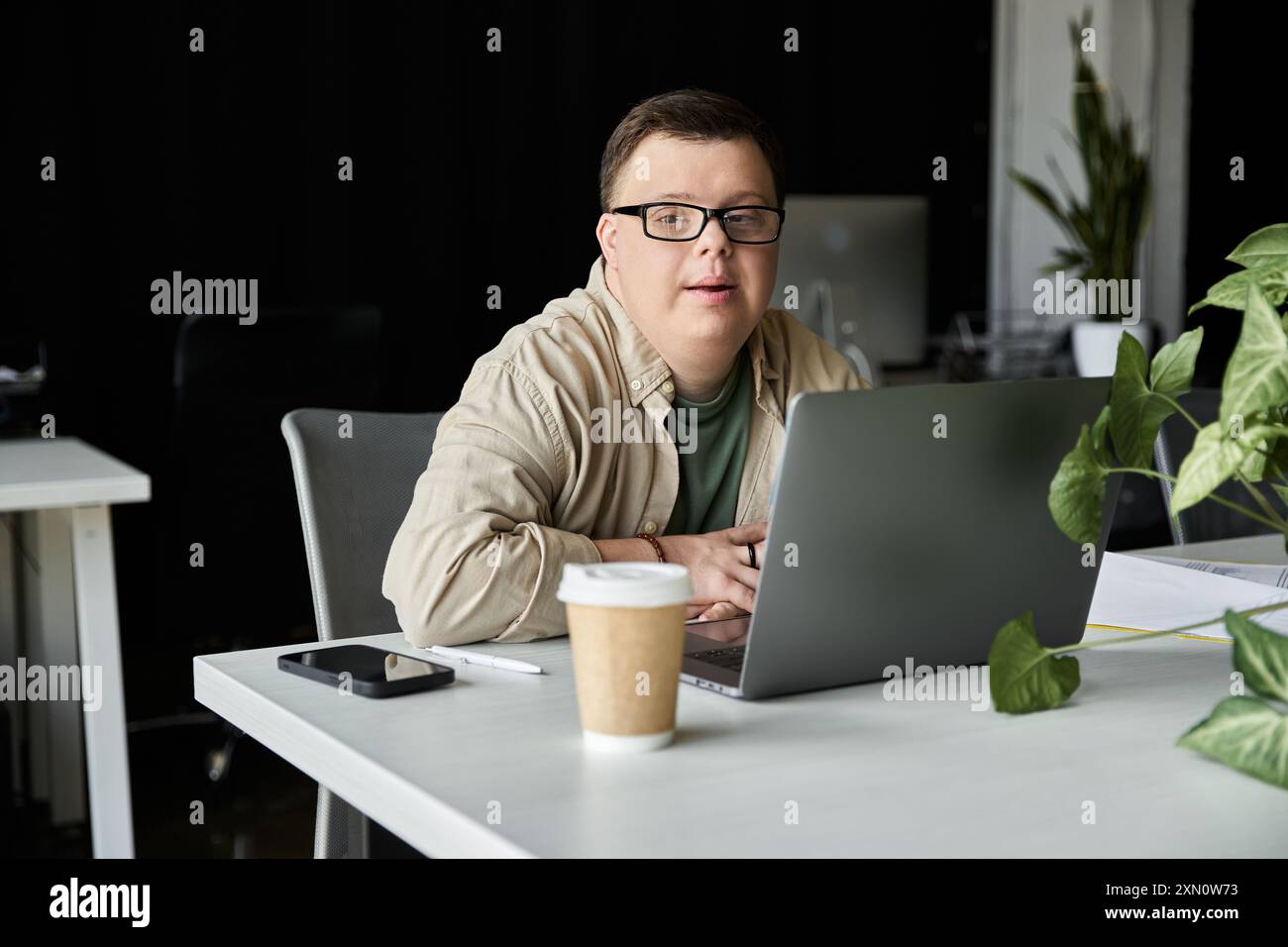 A young man with Down syndrome works on his laptop at a desk Stock ...