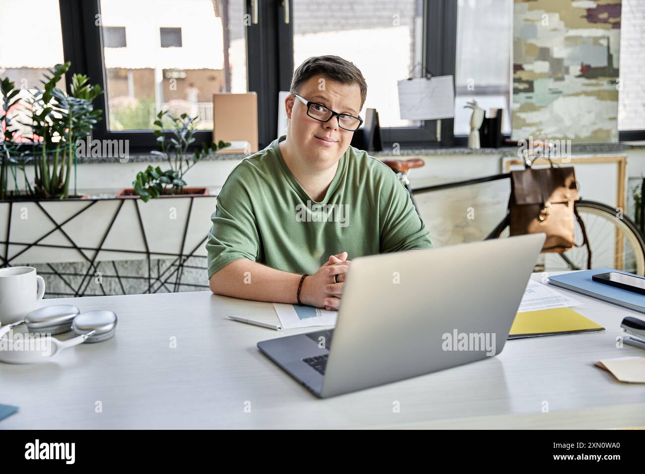 A young man with Down syndrome sits at a desk, smiling while using his ...