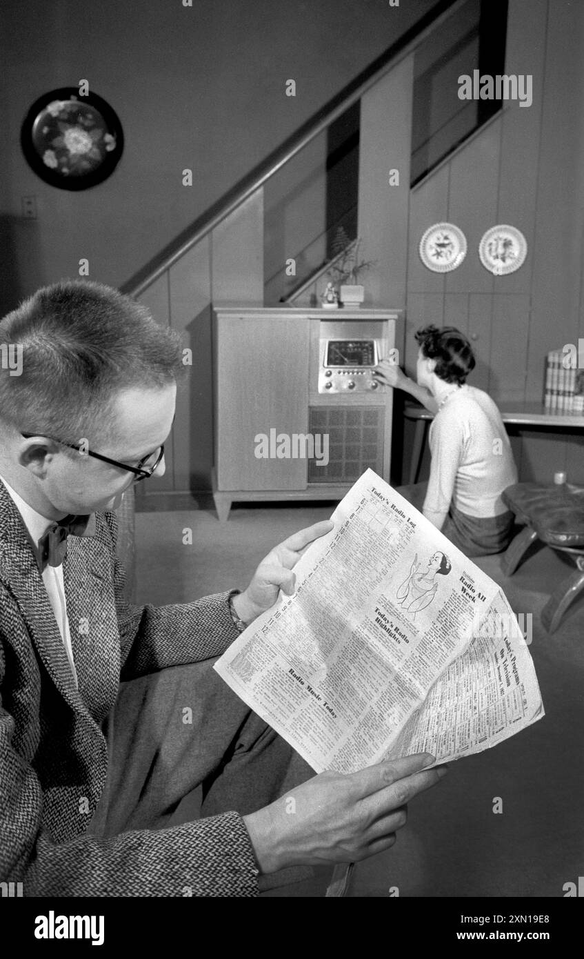 Man reading newspaper while woman is turning radio dial in living room ...