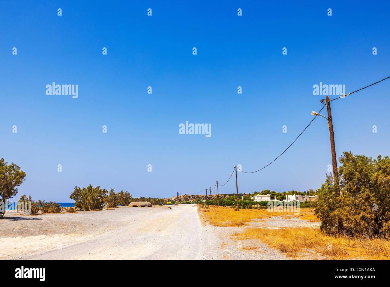 Dirt road along sea with power lines and poles running alongside ...