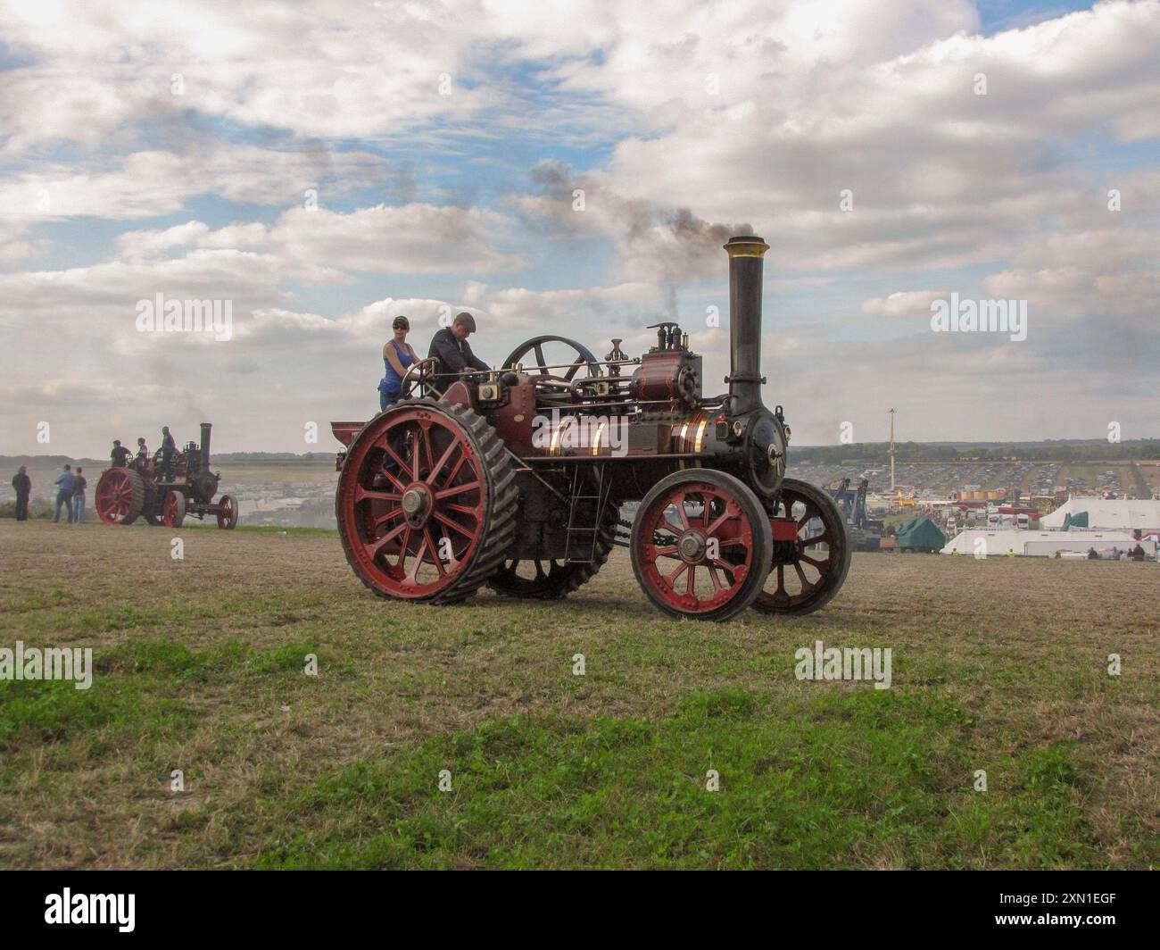 a historic steam engine drives at a field with a plume of smoke at the ...