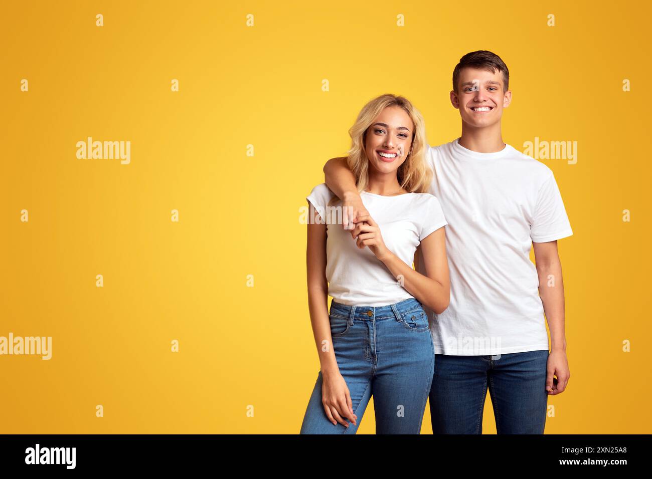 Portrait of happy millennial couple cuddling on yellow studio ...