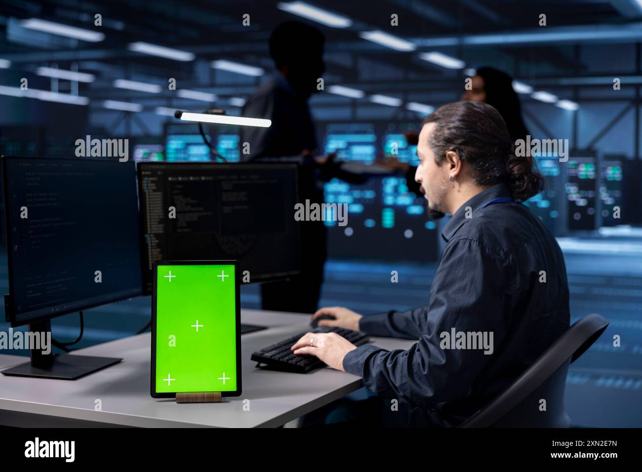 Programmer works on green screen tablet in data center housing storage ...