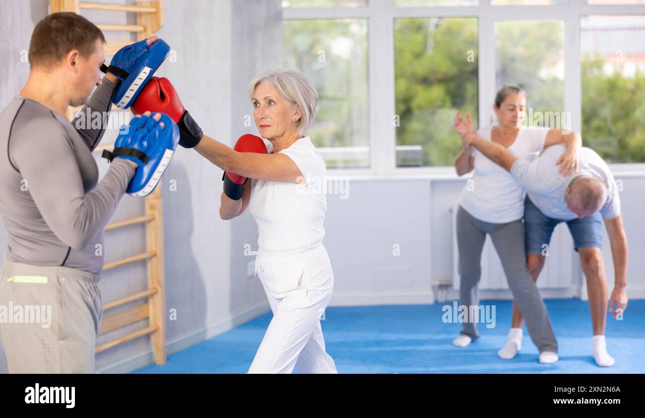 Mature woman with her trainer at gym. Woman wearing boxing gloves ...