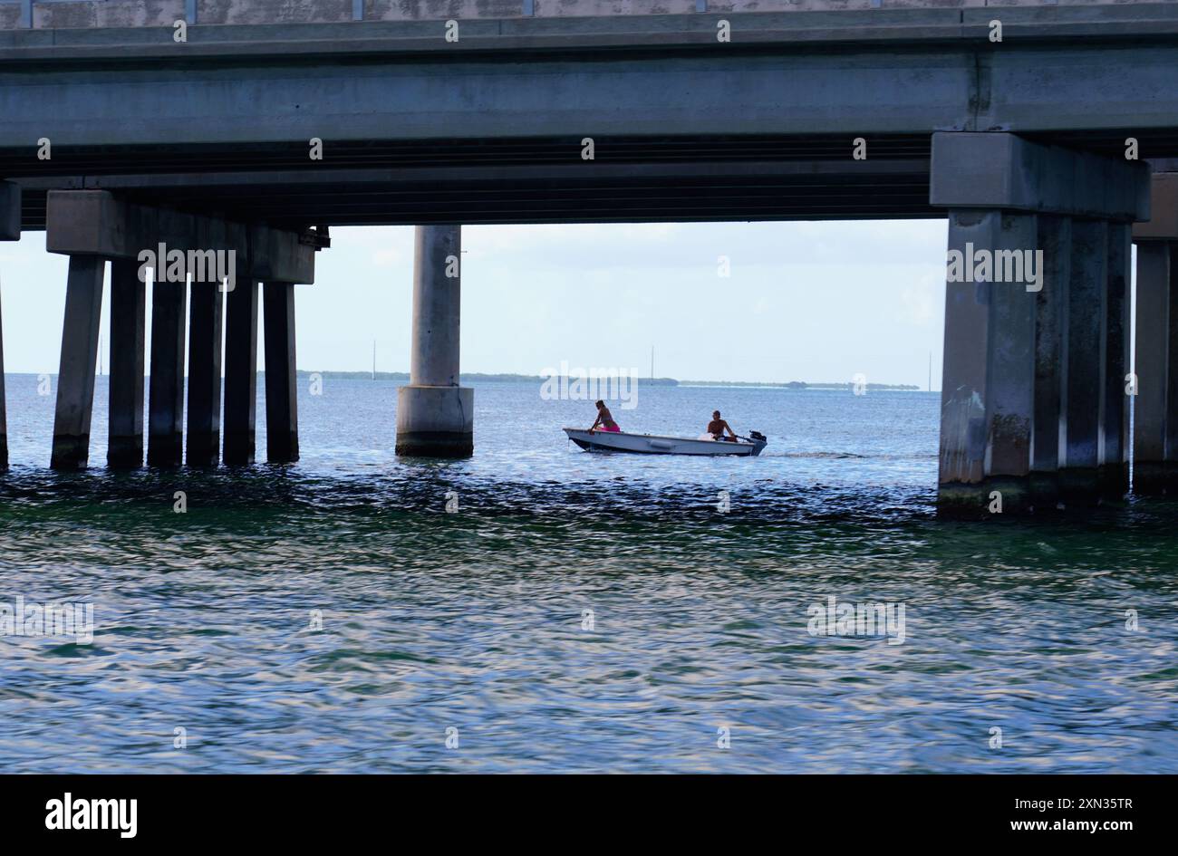 Two people fishing under a bridge in a small boat, enjoying a peaceful ...