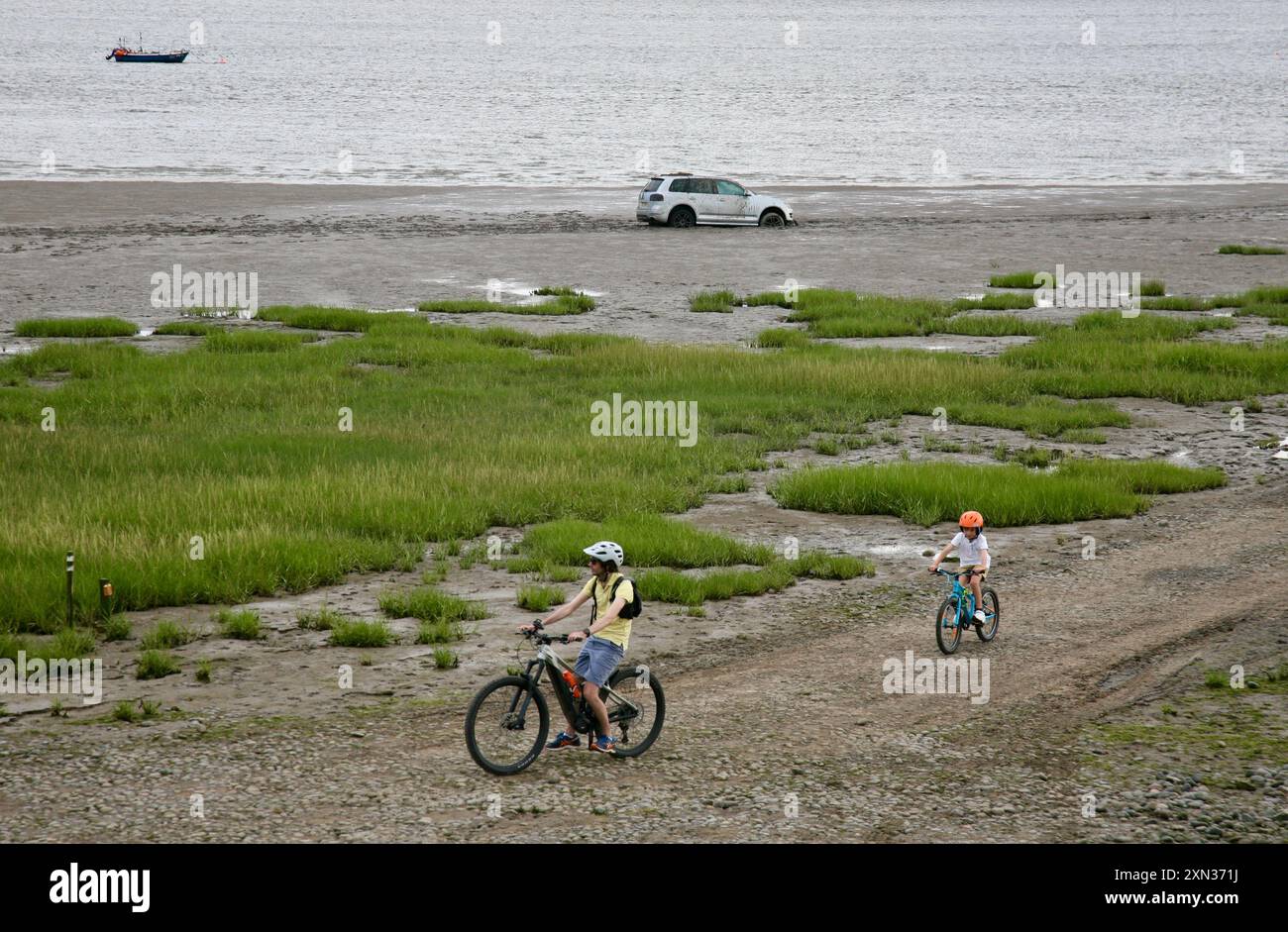 Cyclists on the beach, close to where a motor car has got stuck in ...