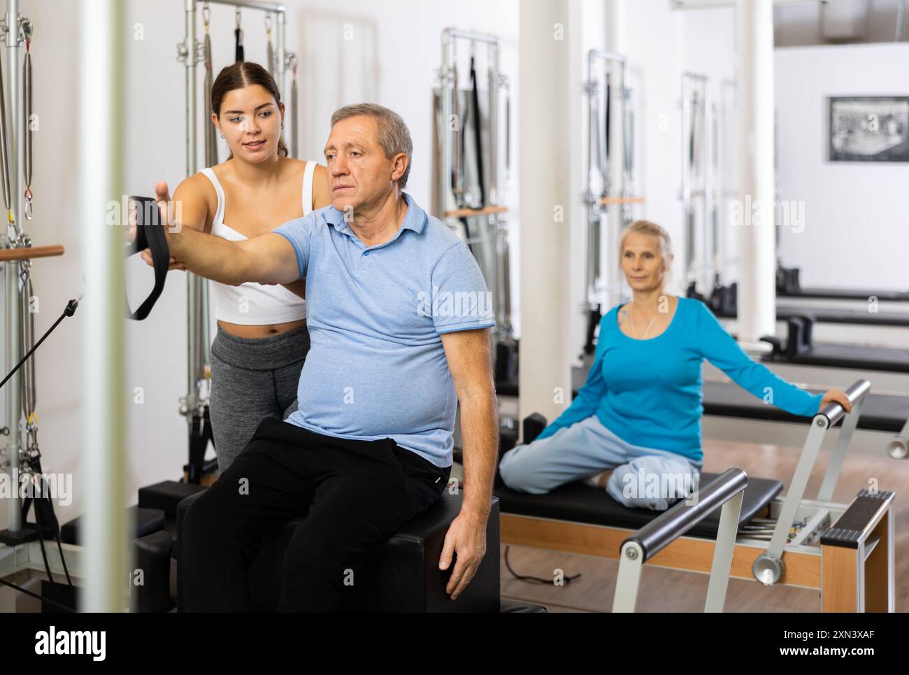 Focused old man practicing stretching Pilates exercise with personal ...