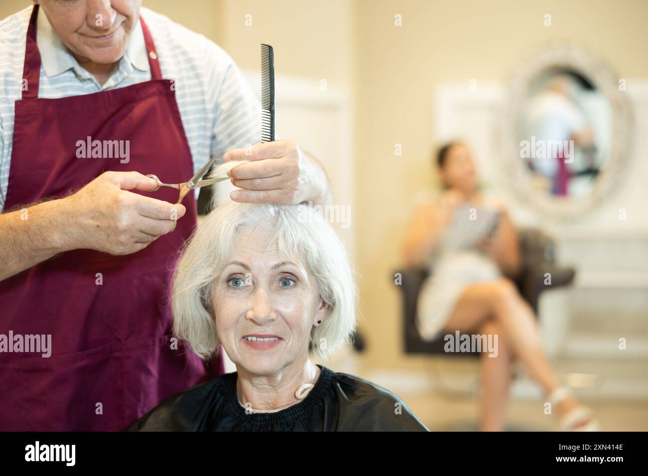 Experienced senior man master makes performs haircut for mature woman ...