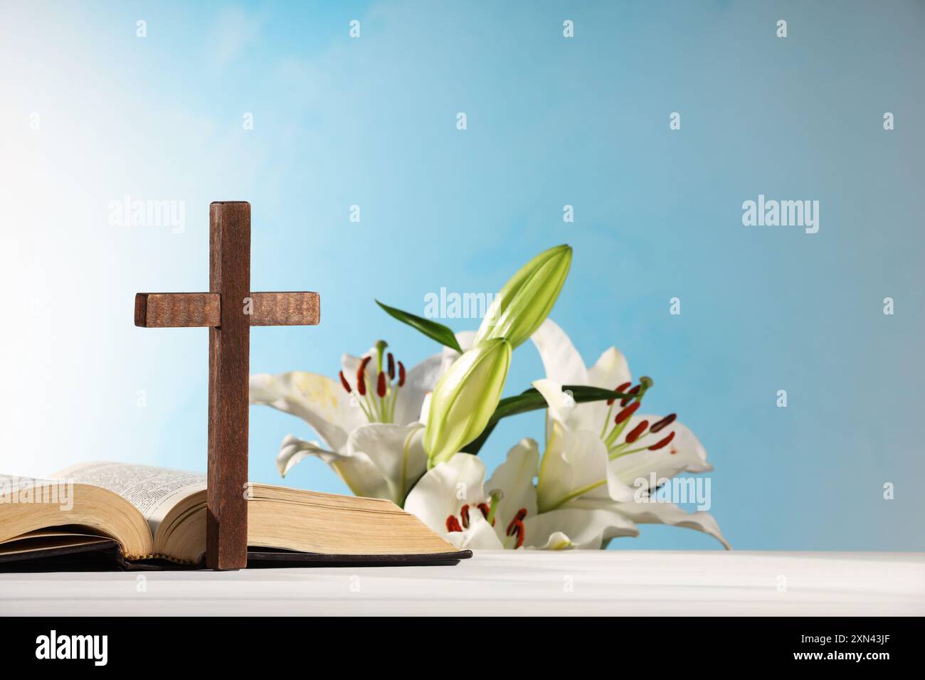 Wooden cross, Bible and beautiful lily flowers on white table against ...