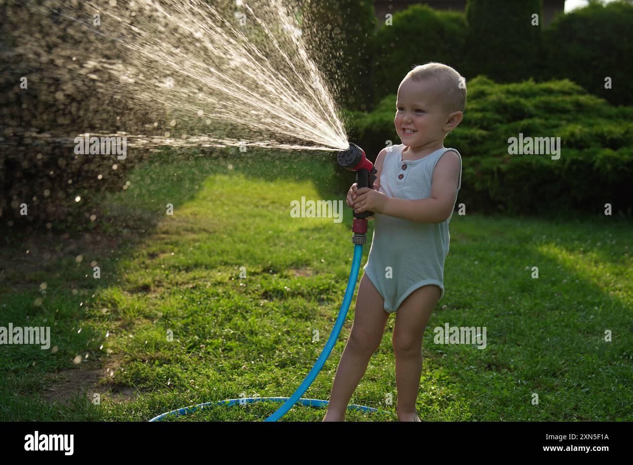 Little boy watering lawn with hose in backyard Stock Photo - Alamy