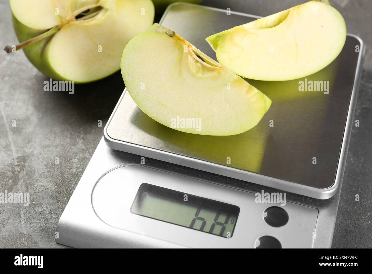Kitchen scale with pieces of apple and fruits on grey textured table ...