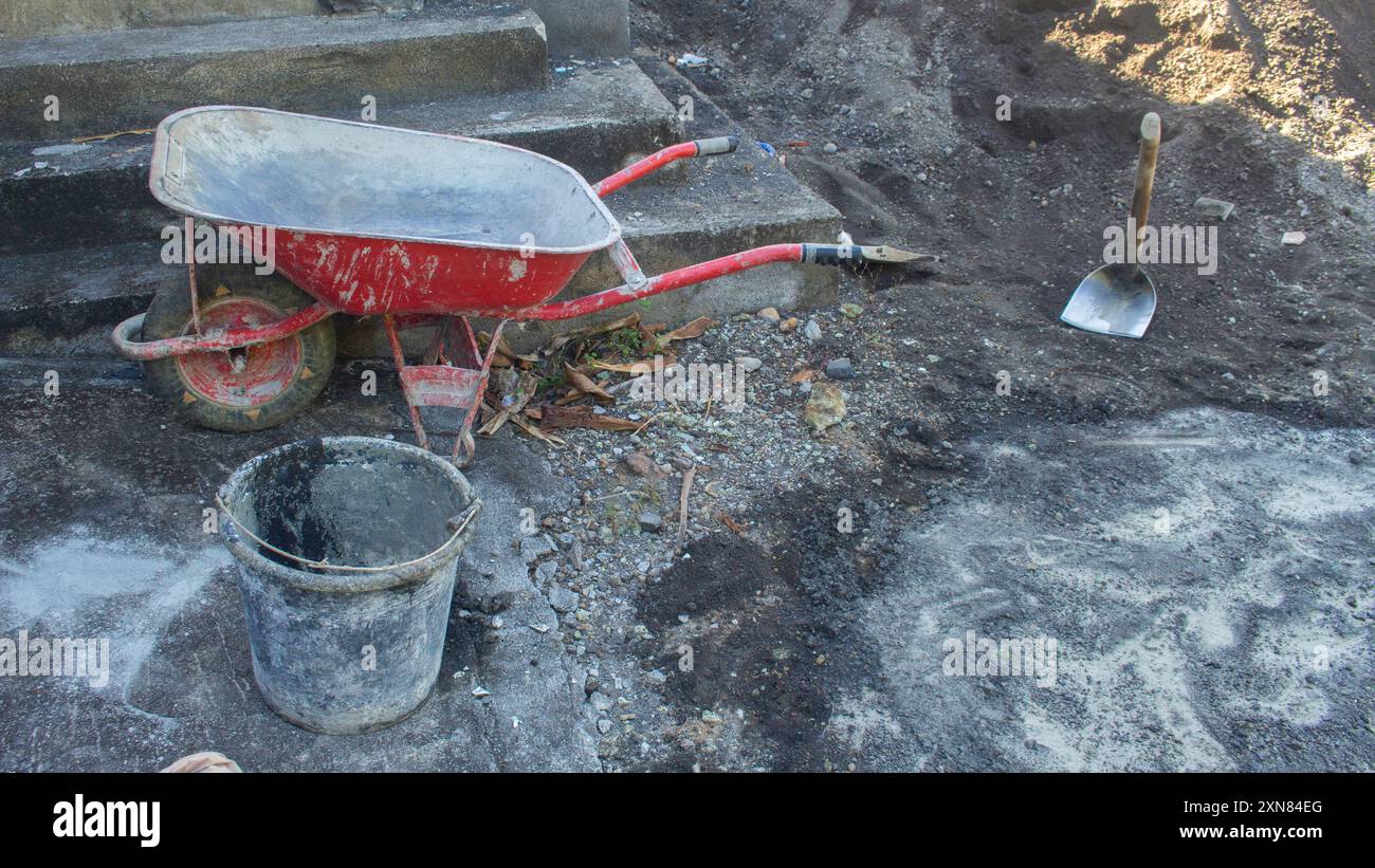 Dirty wheelbarrow, hoe and bucked on black sand for construction tool ...