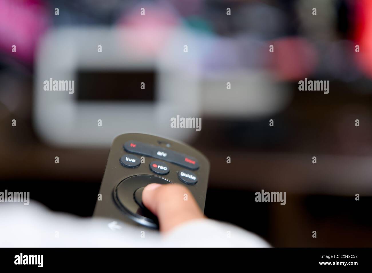 A hand holding a remote control in front of a blurry television screen ...