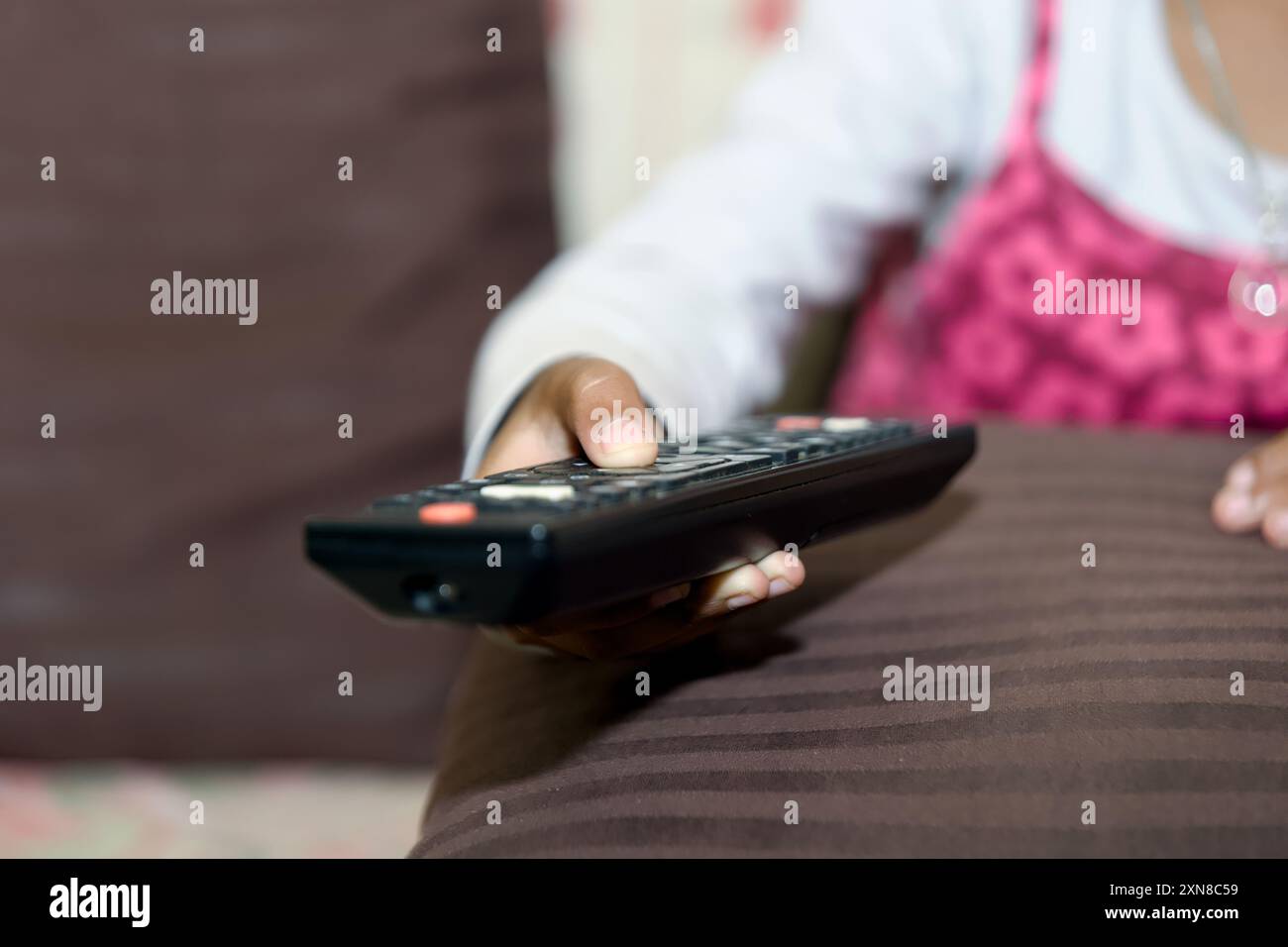 A child's hand navigates the buttons of a TV remote, ready to switch to ...