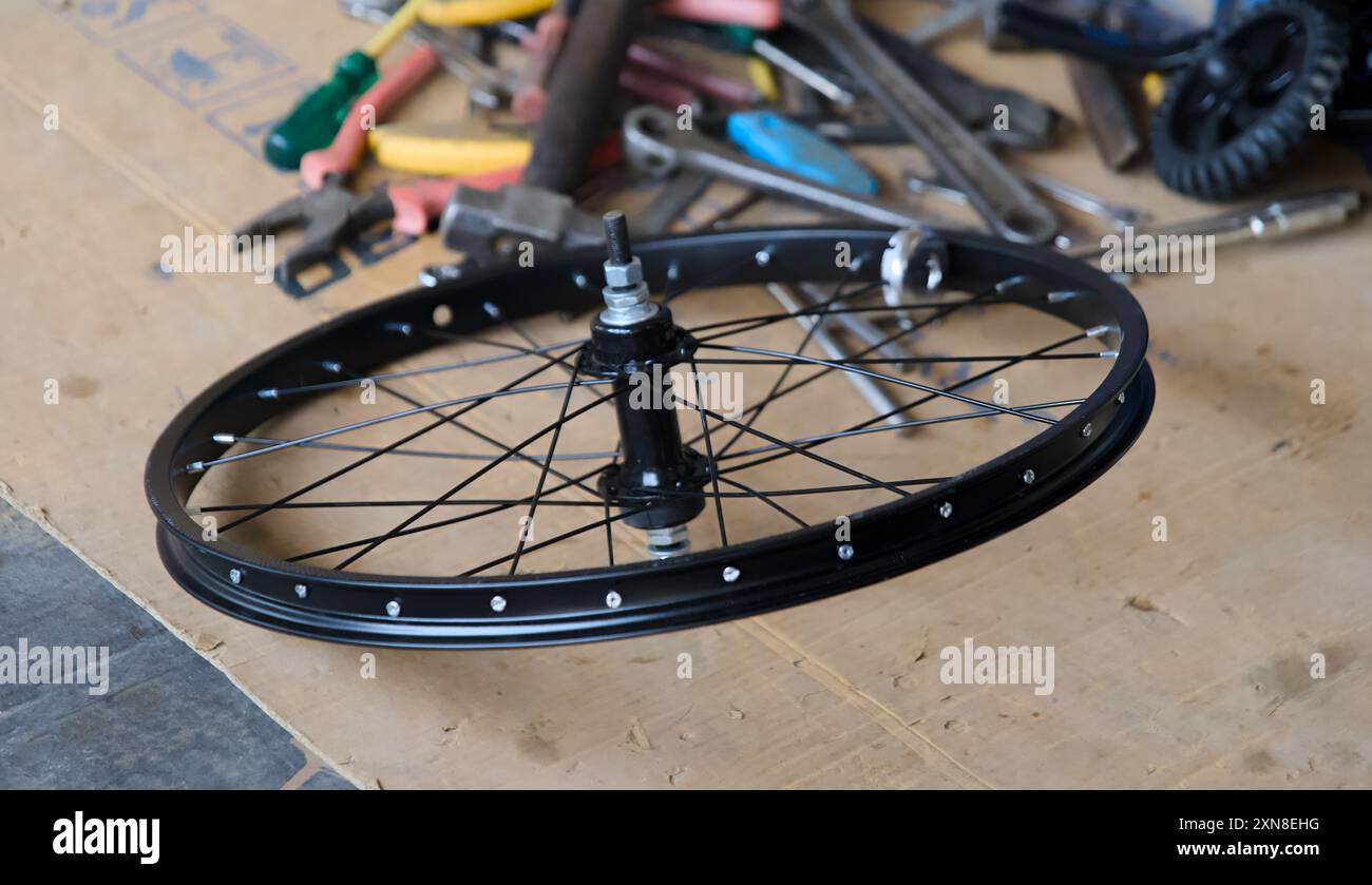 A new bicycle wheel rests on a workshop table surrounded by essential bike repair tools Stock ...