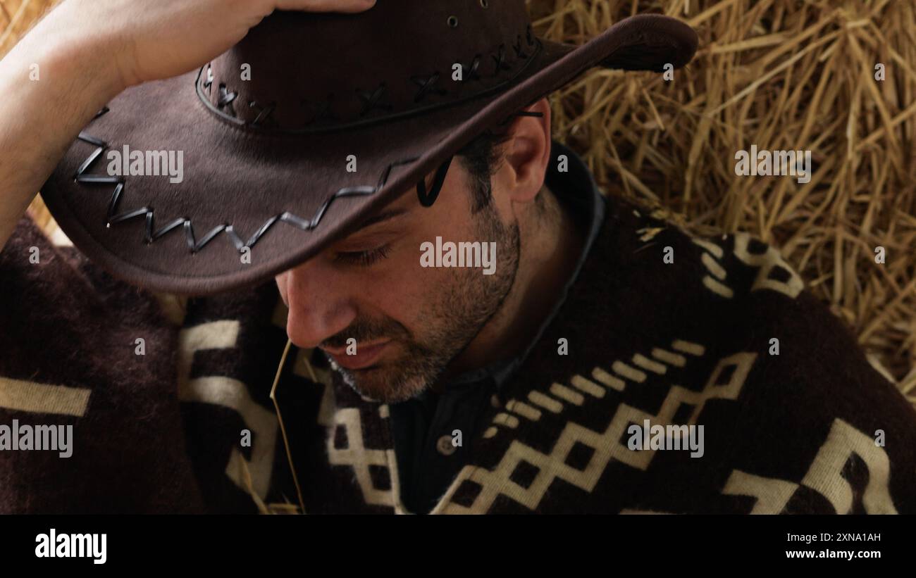 Tired cowboy leaning on hay bale Stock Photo - Alamy