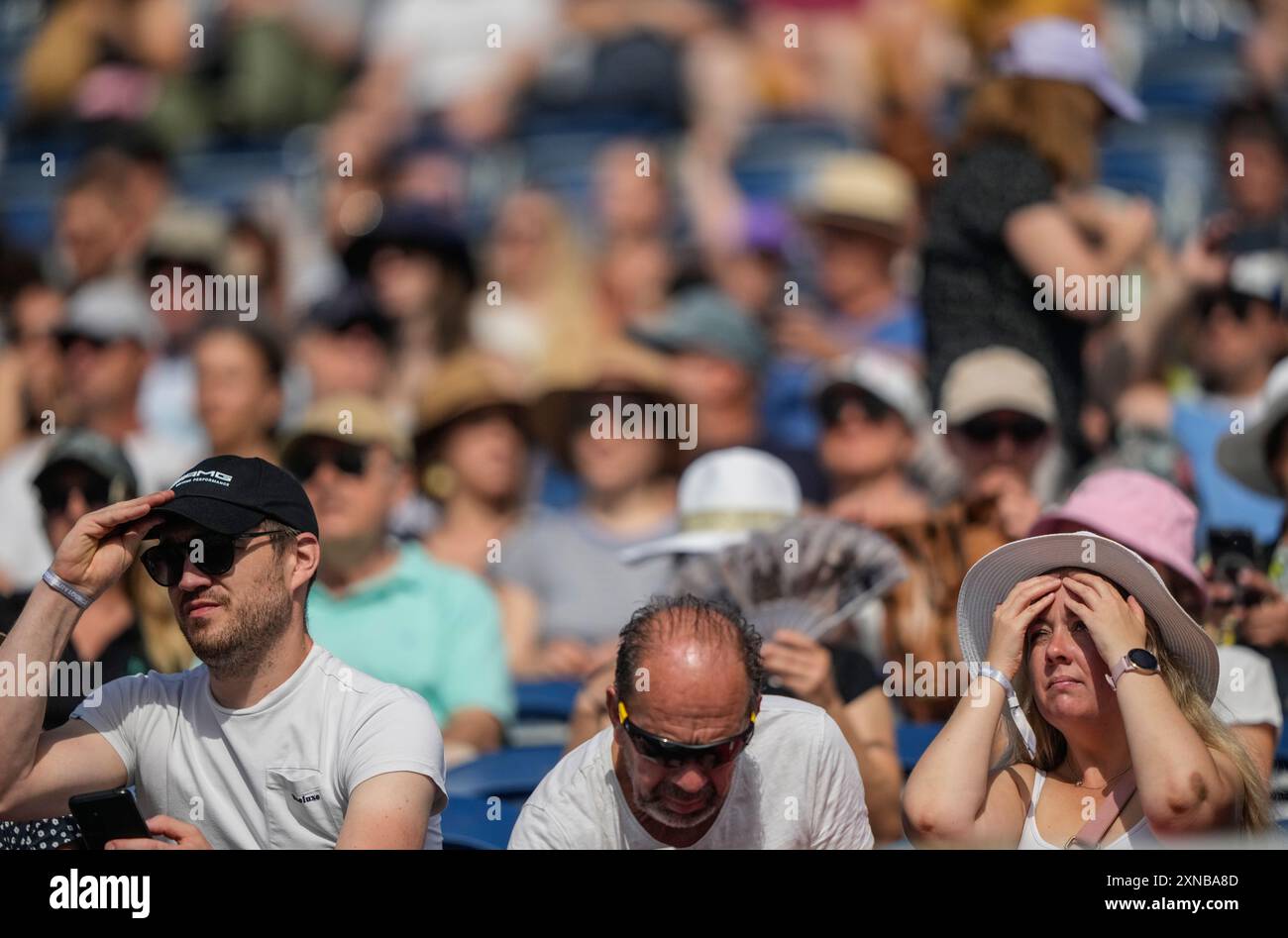 Spectators shelter from sun and apply sunscreen as they watch the ...