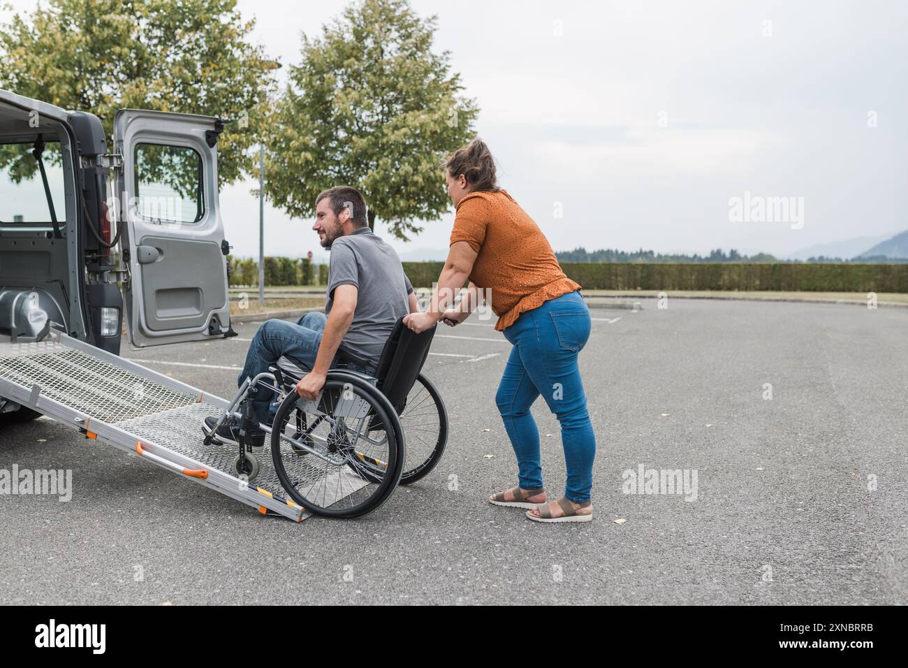 Female assistant helping a male person in wheelchair with transport ...