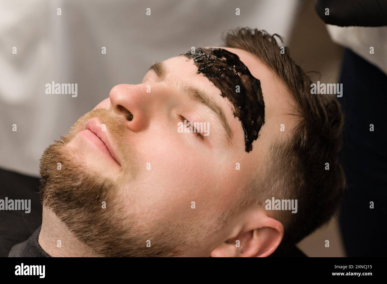 Barber applies a black moisturizing mask to a man's face while shaving ...
