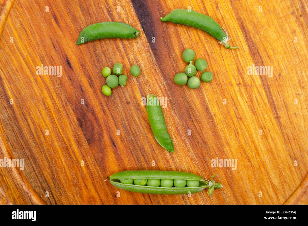 Organic peas and open pea pods in the shape of a funny face on a wooden ...