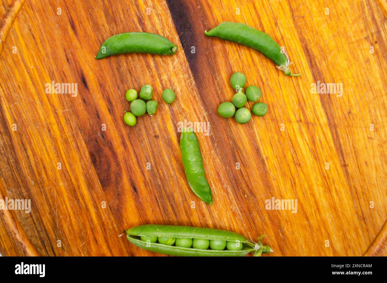 Organic peas and open pea pods in the shape of a funny face on a wooden ...