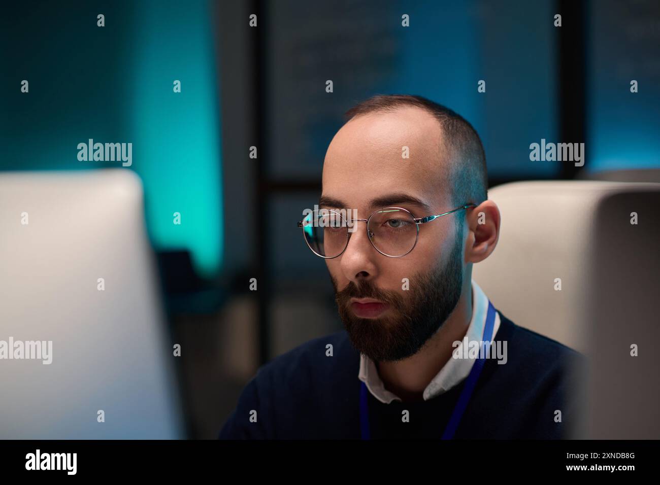 Minimal portrait of bearded computer programmer wearing glasses and looking at screen while ...