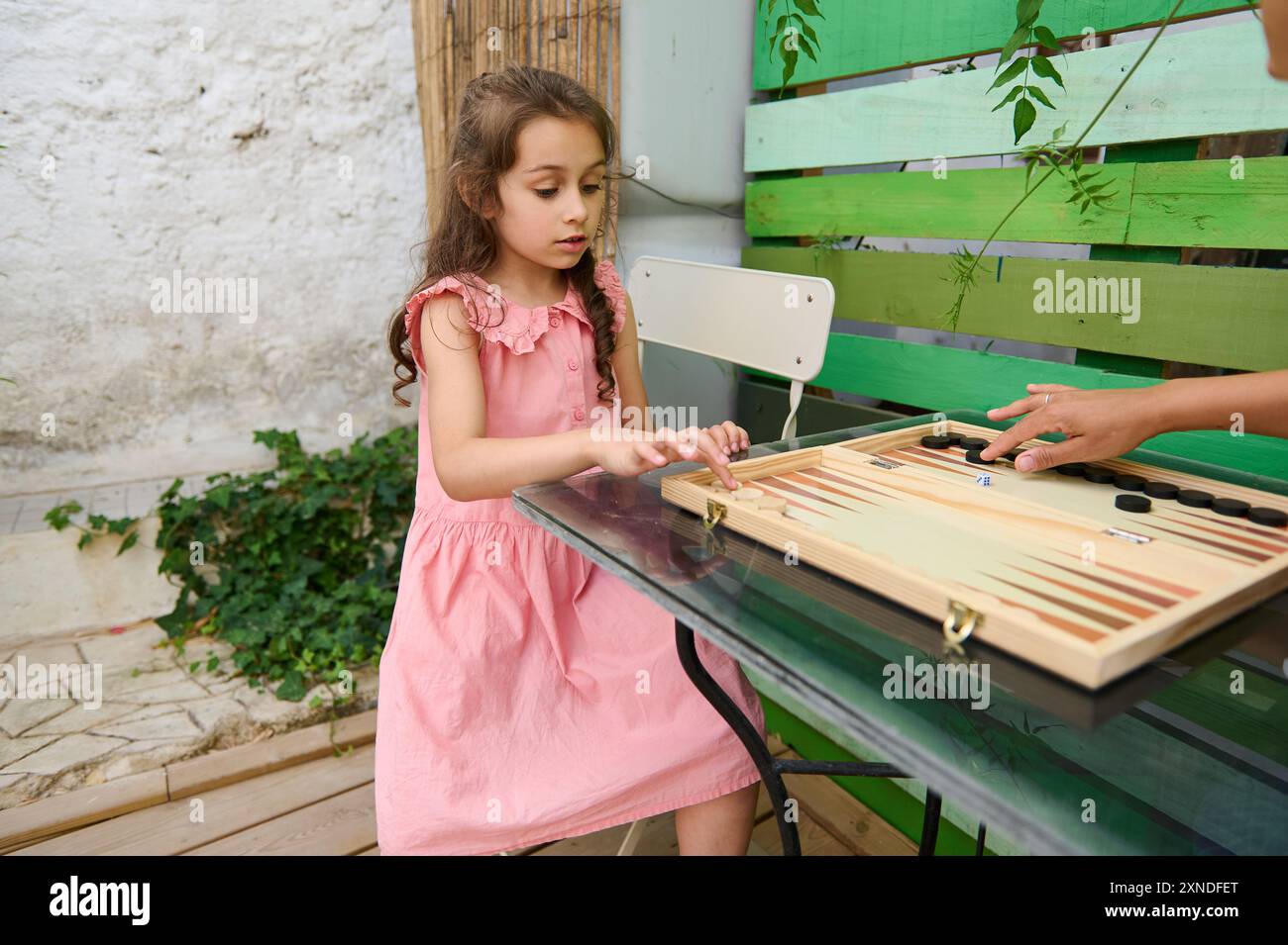 A young girl in a pink dress playing a backgammon game outdoors. The ...
