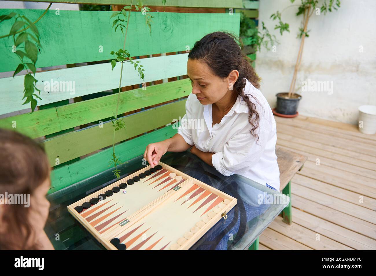 A woman and a child engage in a game of backgammon on an outdoor wooden ...