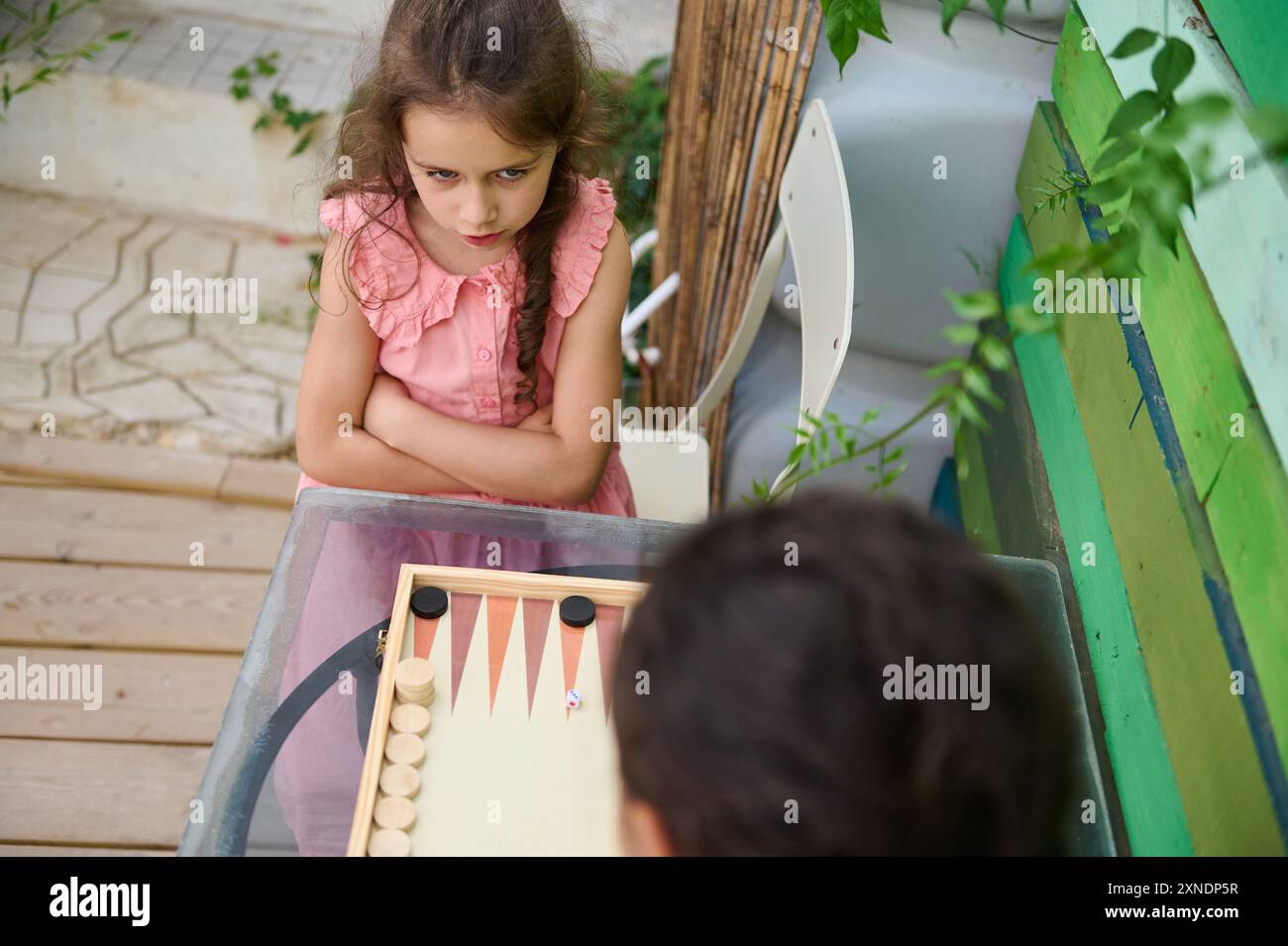 A young girl in a pink dress intensely playing backgammon with a friend ...