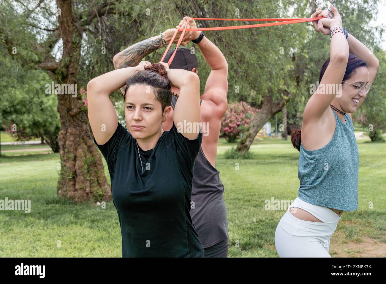 Three friends work out using resistance bands in a green park, staying ...