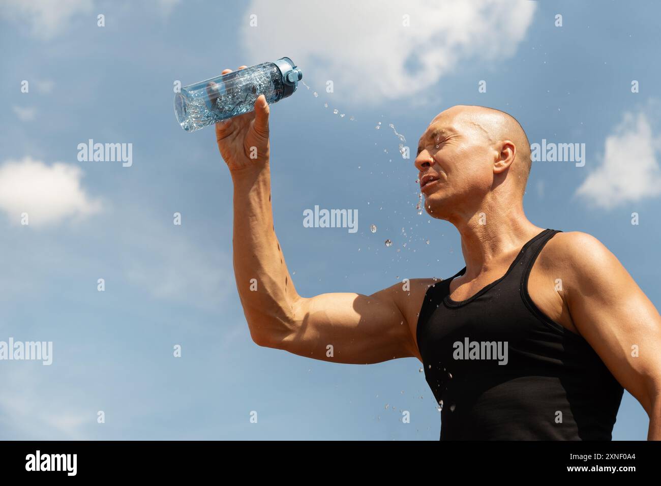 Sweaty handsome sporty man refreshing himself water from bottle against ...