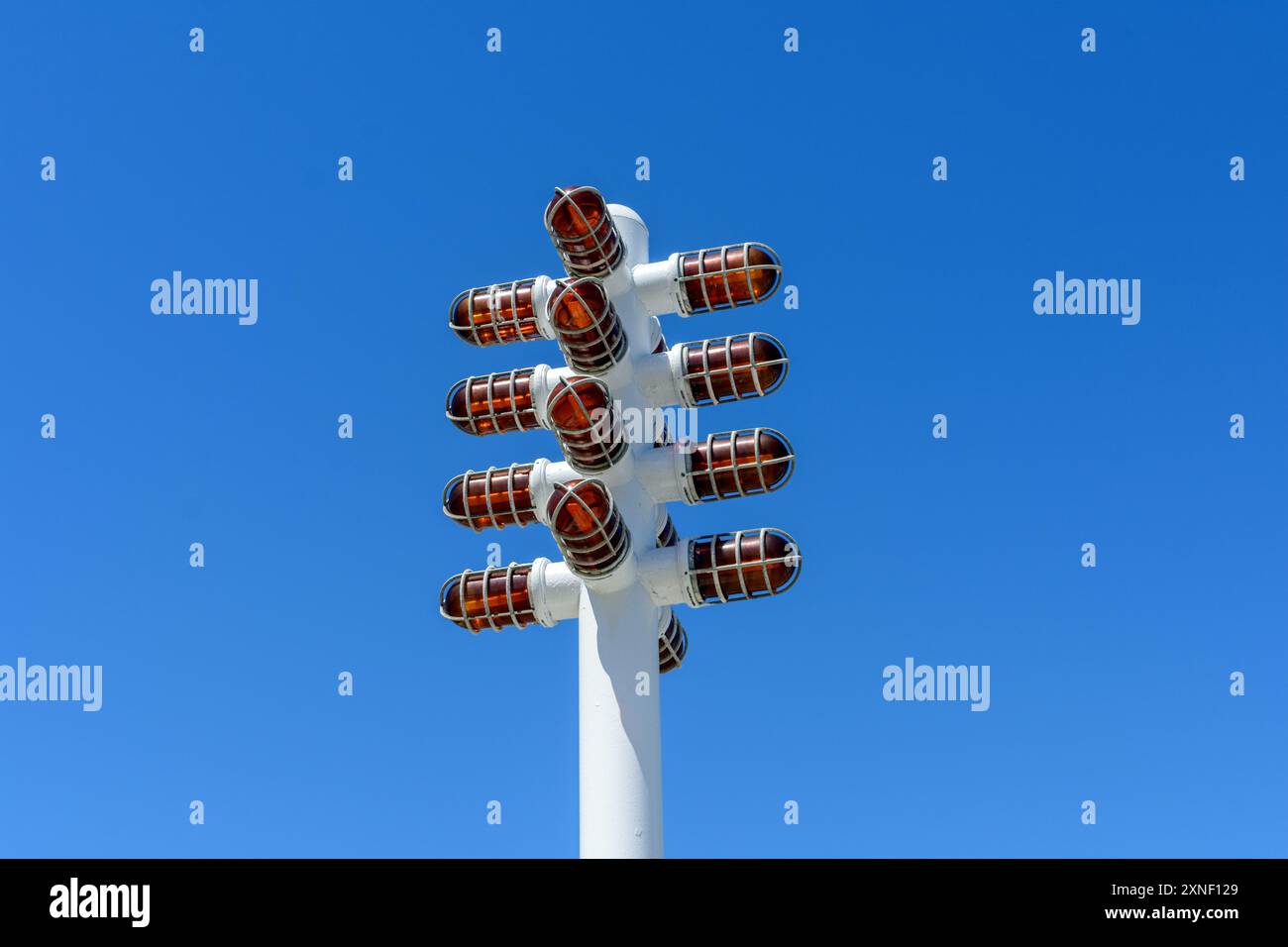 A white pole with multiple red-caged lights stands against a clear blue ...