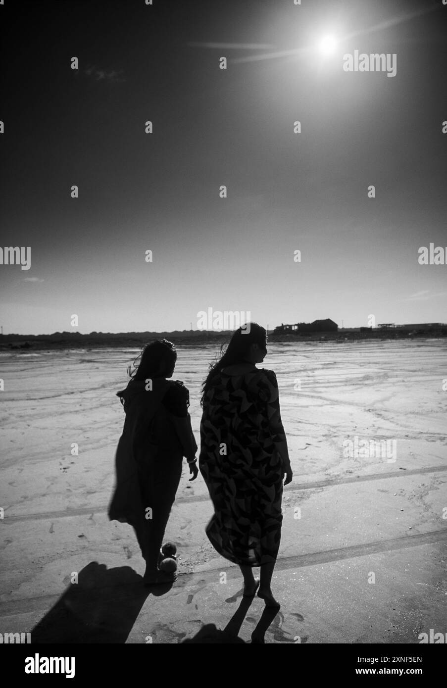 Two Wayuu women walking on the shore of the Maracaibo Lake at sunset ...