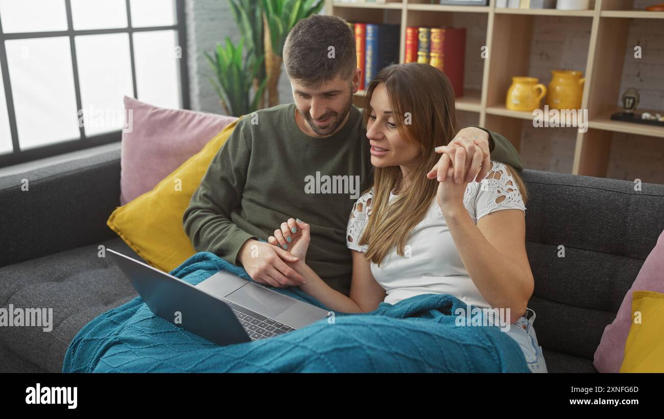 A man and woman cuddle on a couch under a blanket with a laptop in a ...
