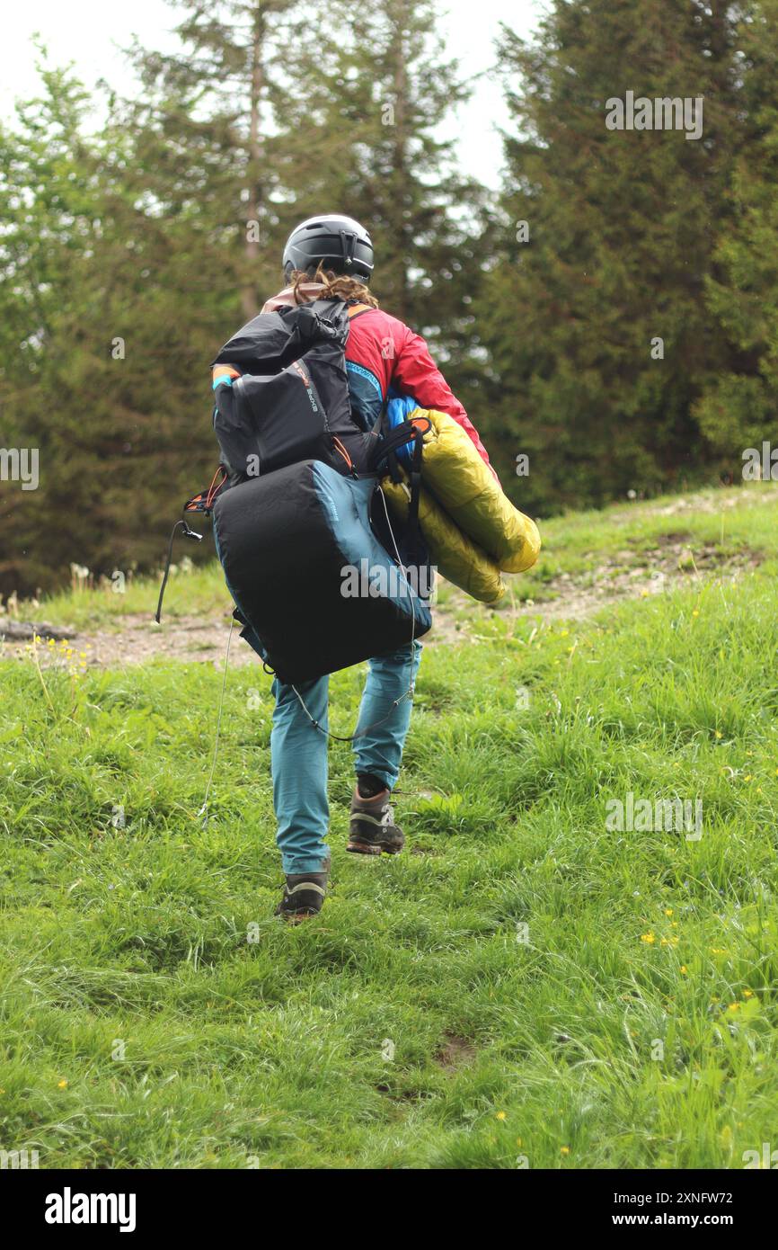 A female paraglider walks uphill, carrying her gear and getting ready ...