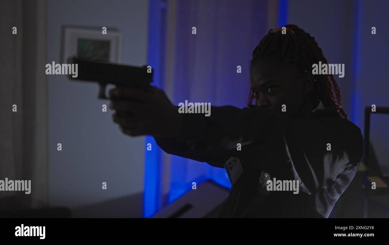 Armed african american woman aiming a gun in a dimly lit room, creating ...
