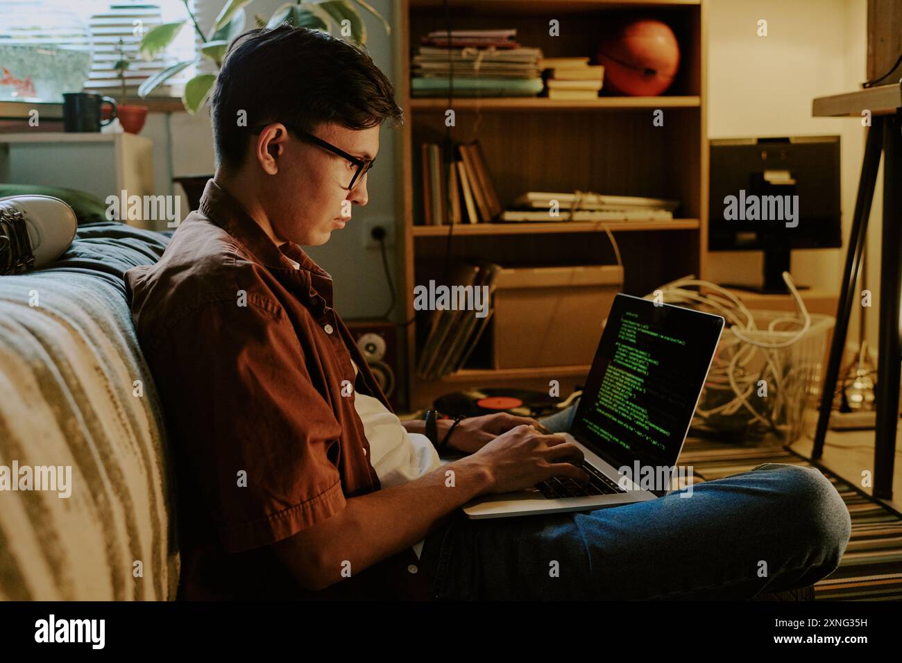 Student sitting on floor in lotus position while writing codes for his personal application ...