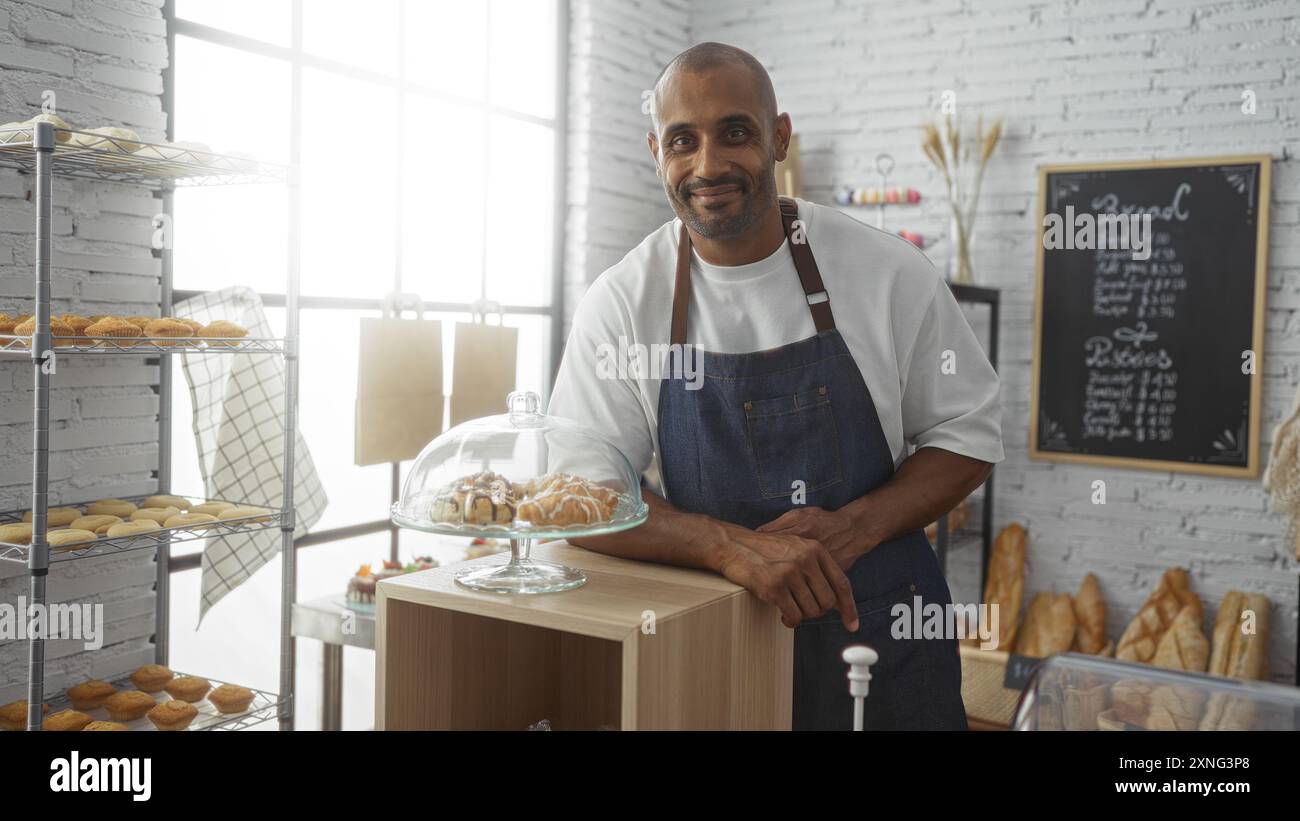 Handsome man in a bakery wearing an apron, standing next to a display ...
