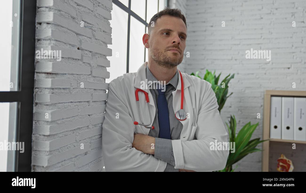 Confident male doctor with folded arms standing in a clinic room ...