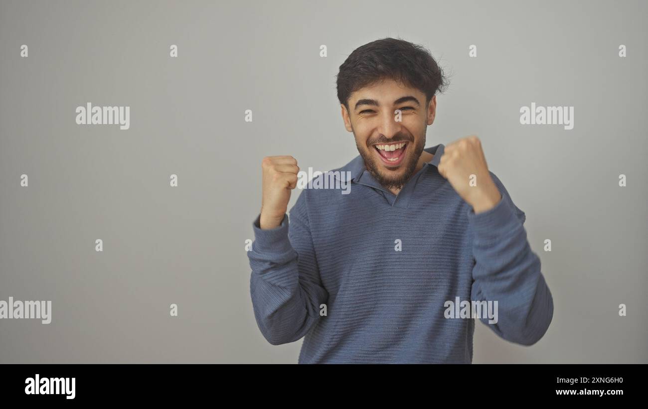 A cheerful young arab man with a beard celebrating and clenching fists ...