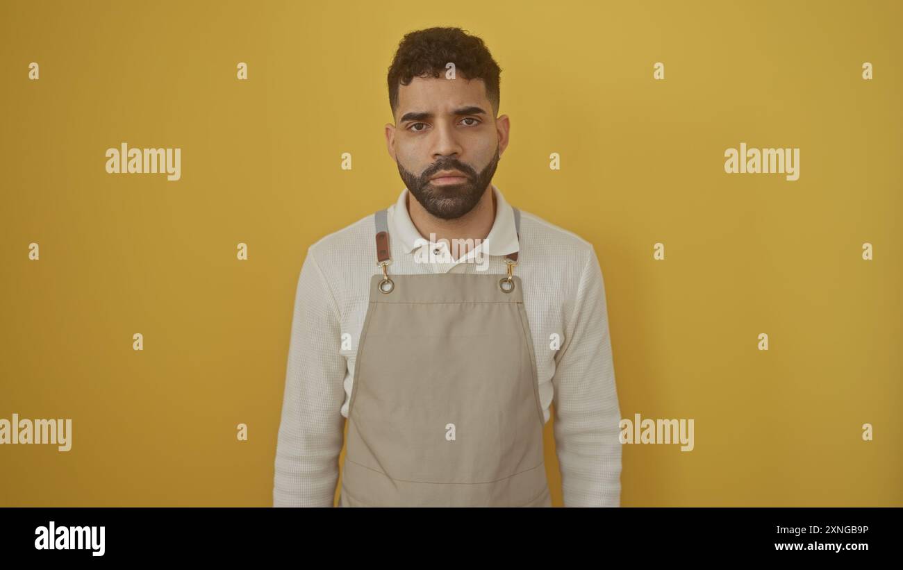 A young hispanic man wearing an apron poses against an isolated yellow ...