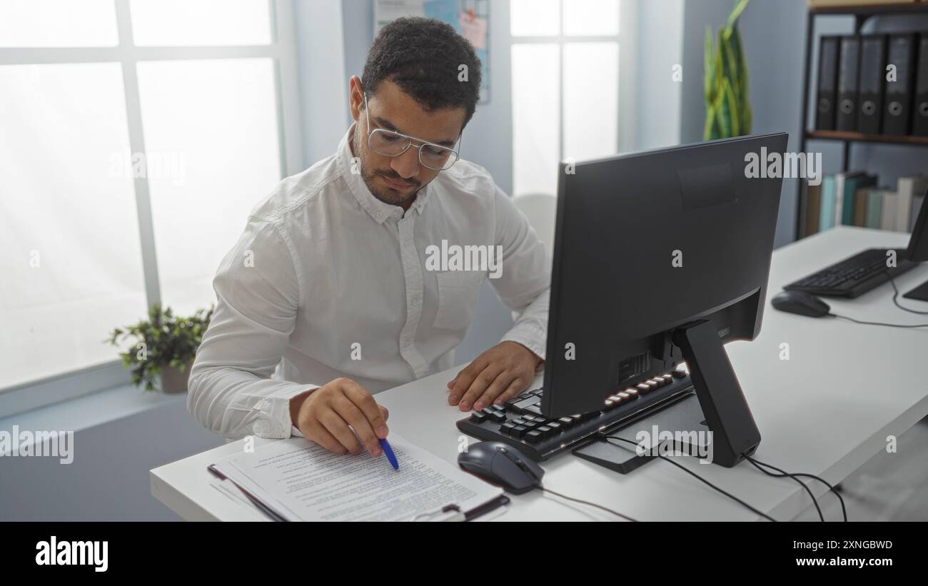 Hispanic man working at a desk in an office with a computer and ...